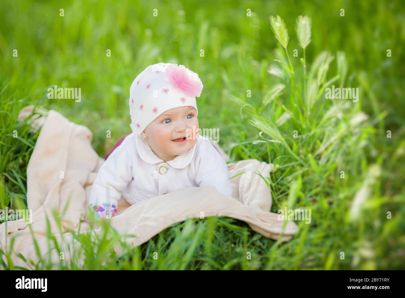 Smiling happy baby girl sitting on green grass in the park. Children ...