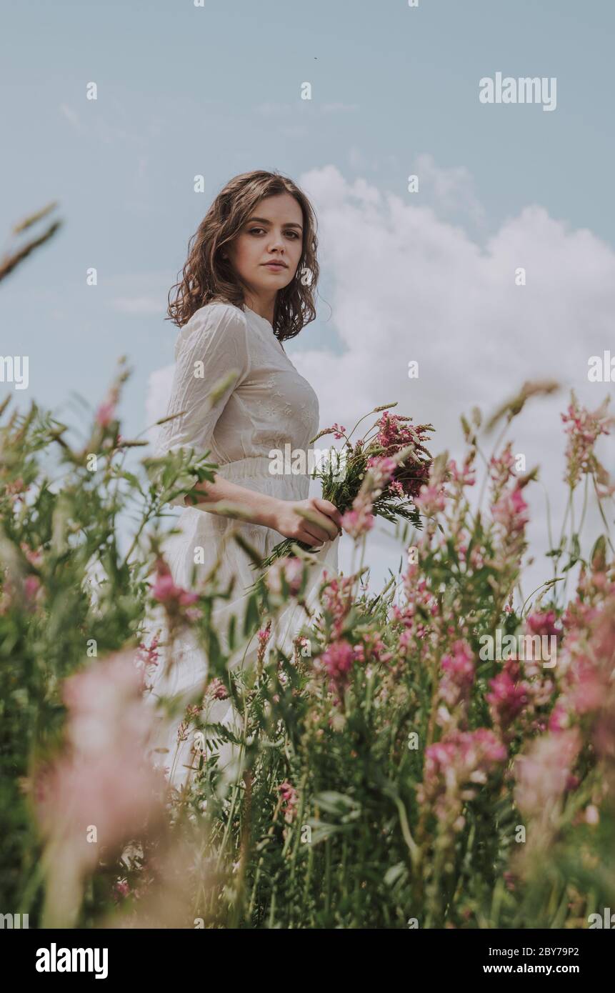 Low angle side view portrait of young woman in white dress looking with ...