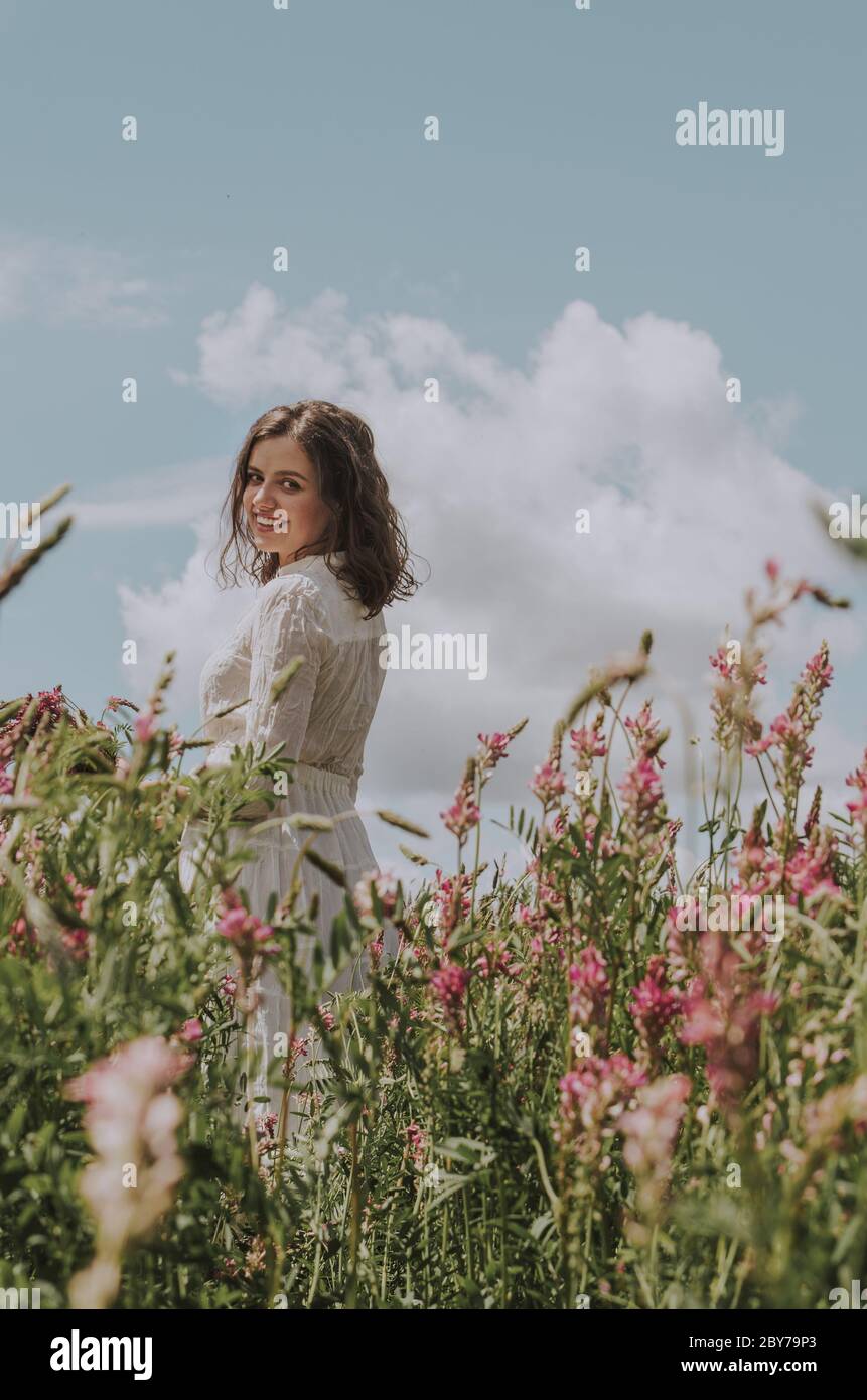 Low angle side view portrait of young woman in white dress smiling at ...