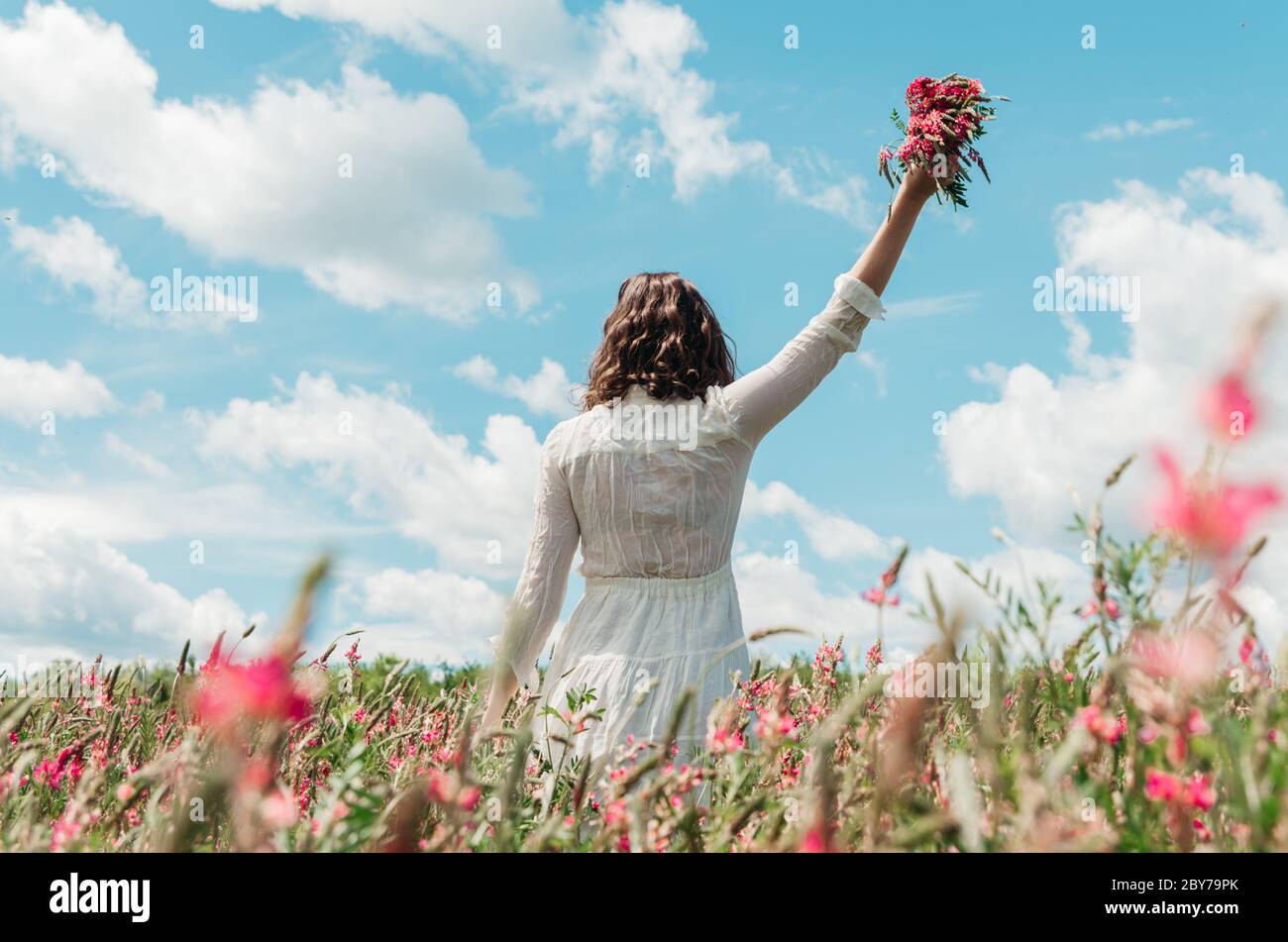 Back view portrait of young woman in motion in a long white dress ...