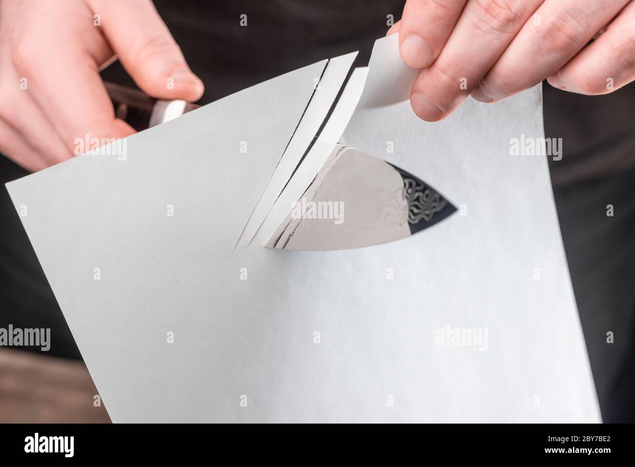 Man cutting a thin paper sheet to test sharpness of blade Stock Photo ...
