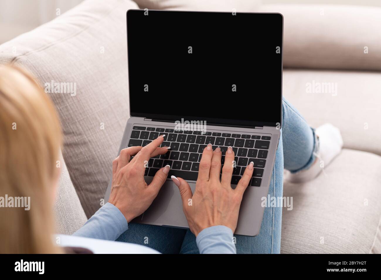 Work on couch. Woman is typing on laptop with blank screen, sitting on ...