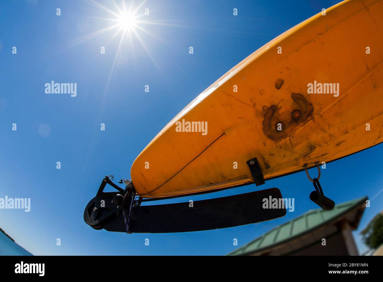 Close up from view under yellow kayak in wooden stand with blue sky and ...