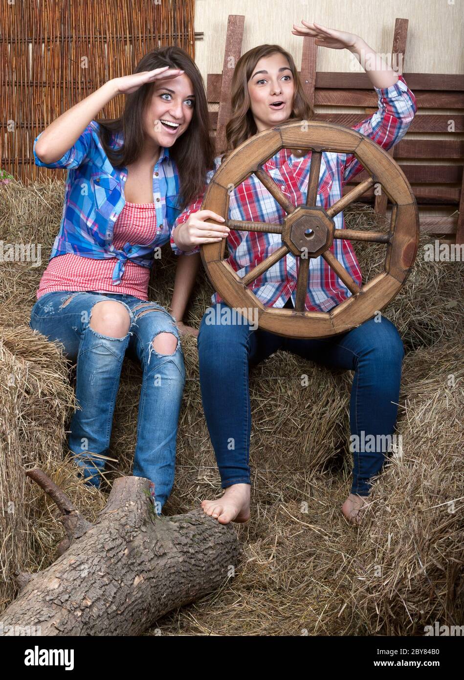 Two beautiful girls in the hay with a wheel on the wagon Stock Photo ...