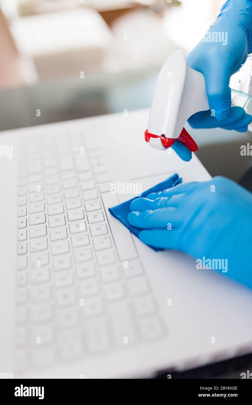 Woman wearing medical rubber gloves wiping laptop keyboard with small ...