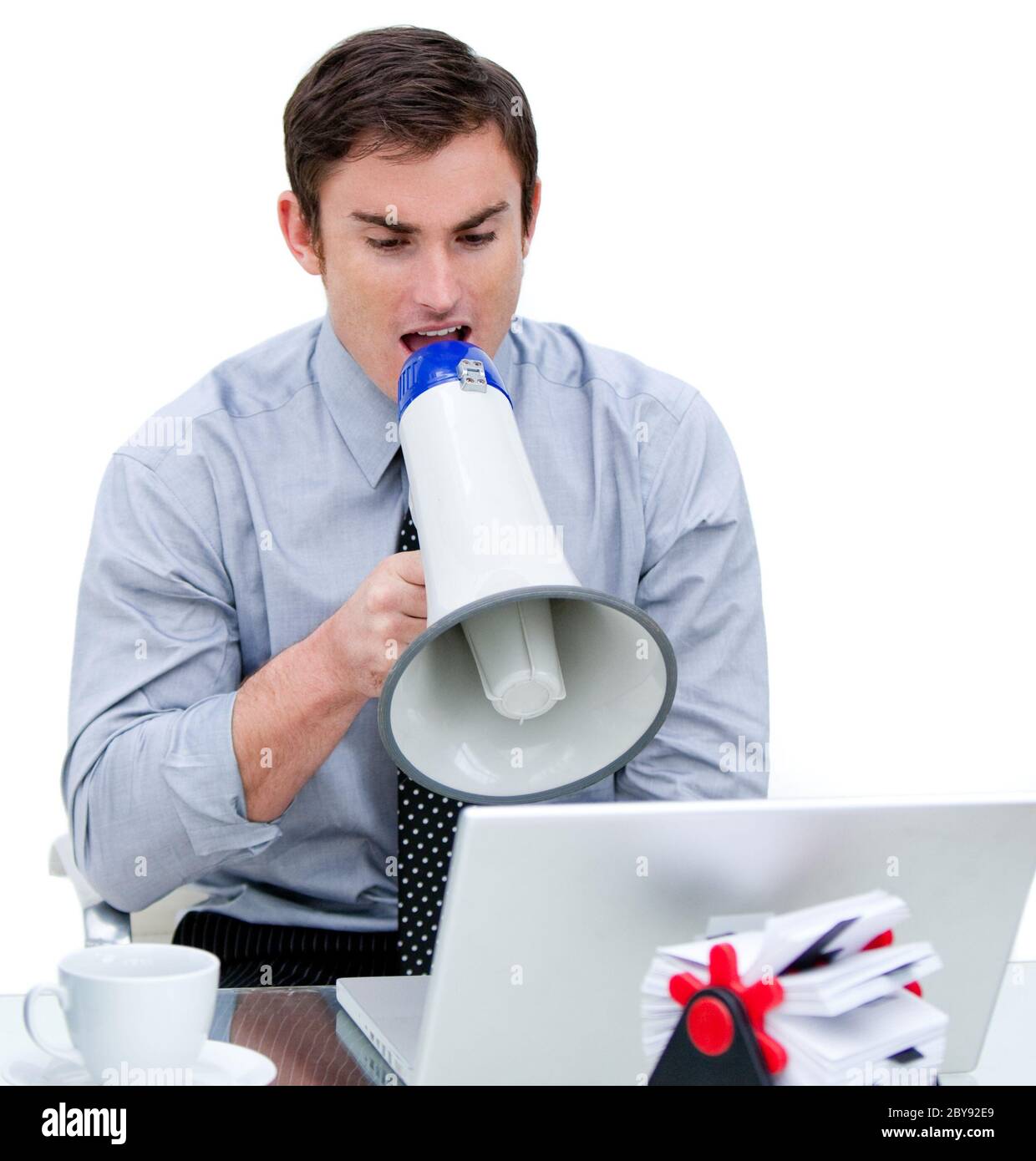 Angry businessman yelling through a megaphone sitting at his desk in ...