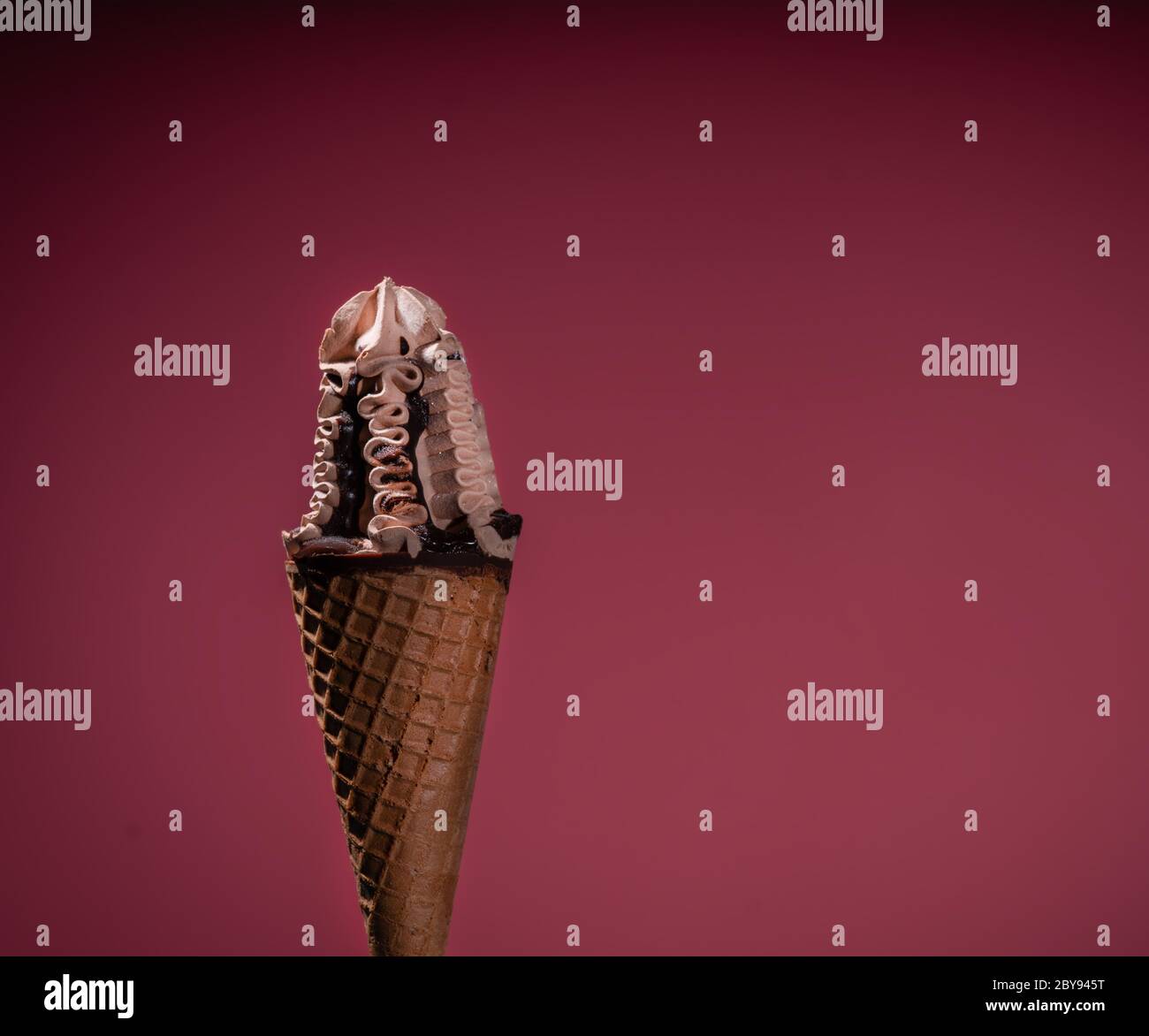 Chocolate ice cream in a wafer cone placed to the side over a maroon ...