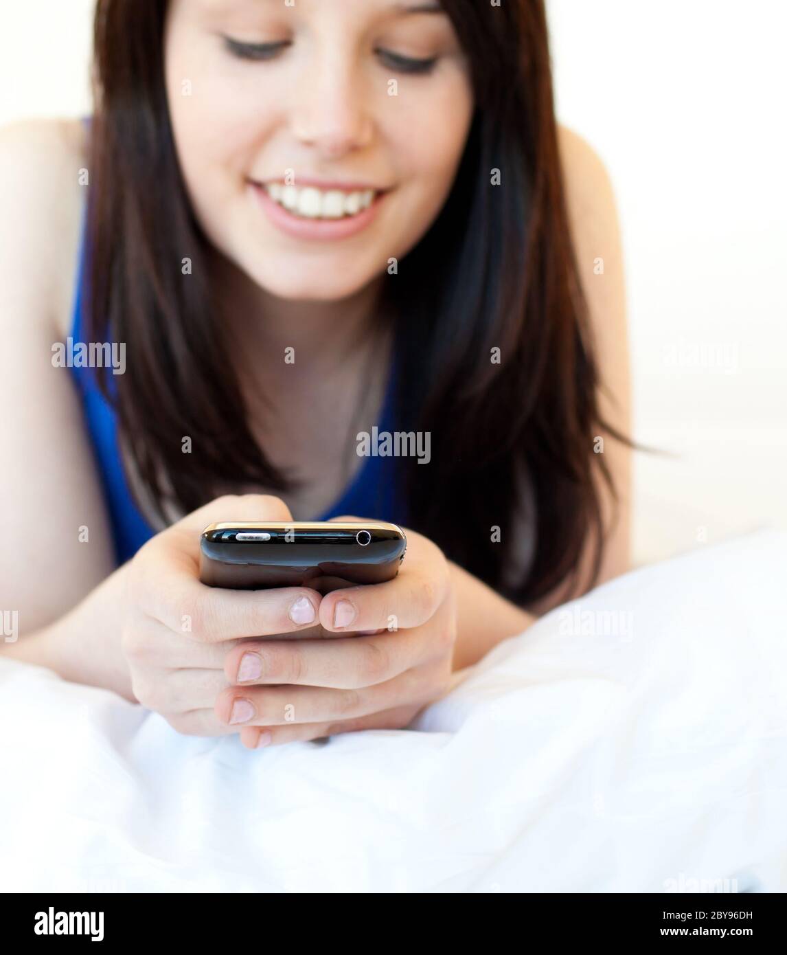 Radiant young woman texting while lying on a bed Stock Photo - Alamy