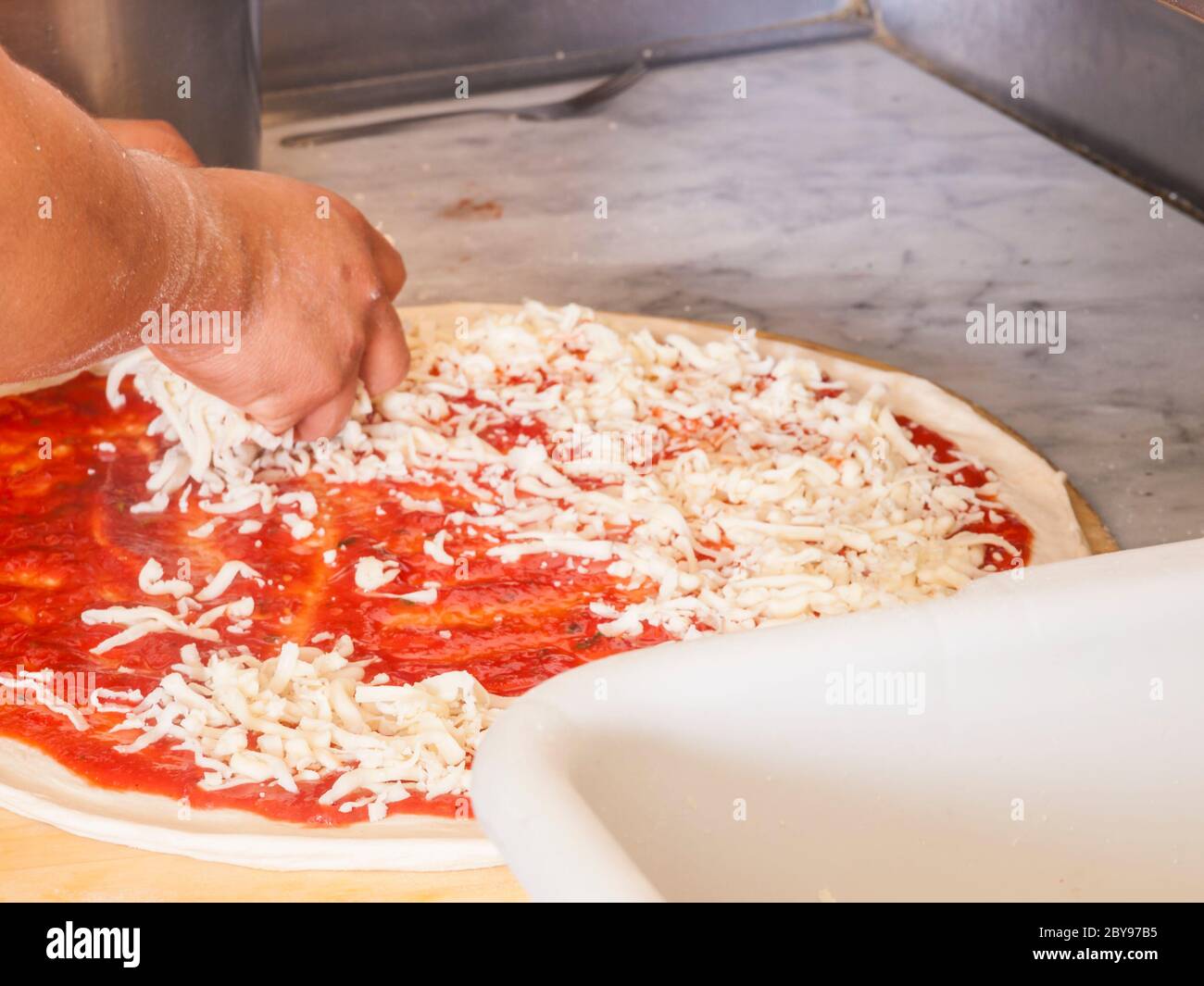 Pizza and pizza making hands laying down shredded mozzarella cheese on ...