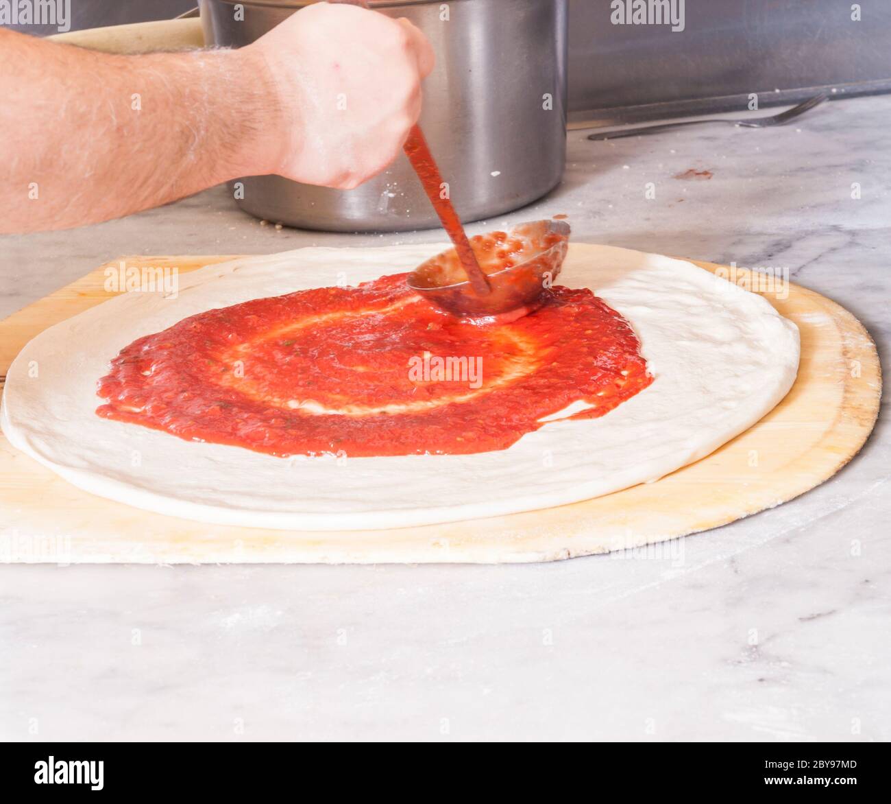 Pizza and pizza making hand putting spreading sauce on a pizza from a ...