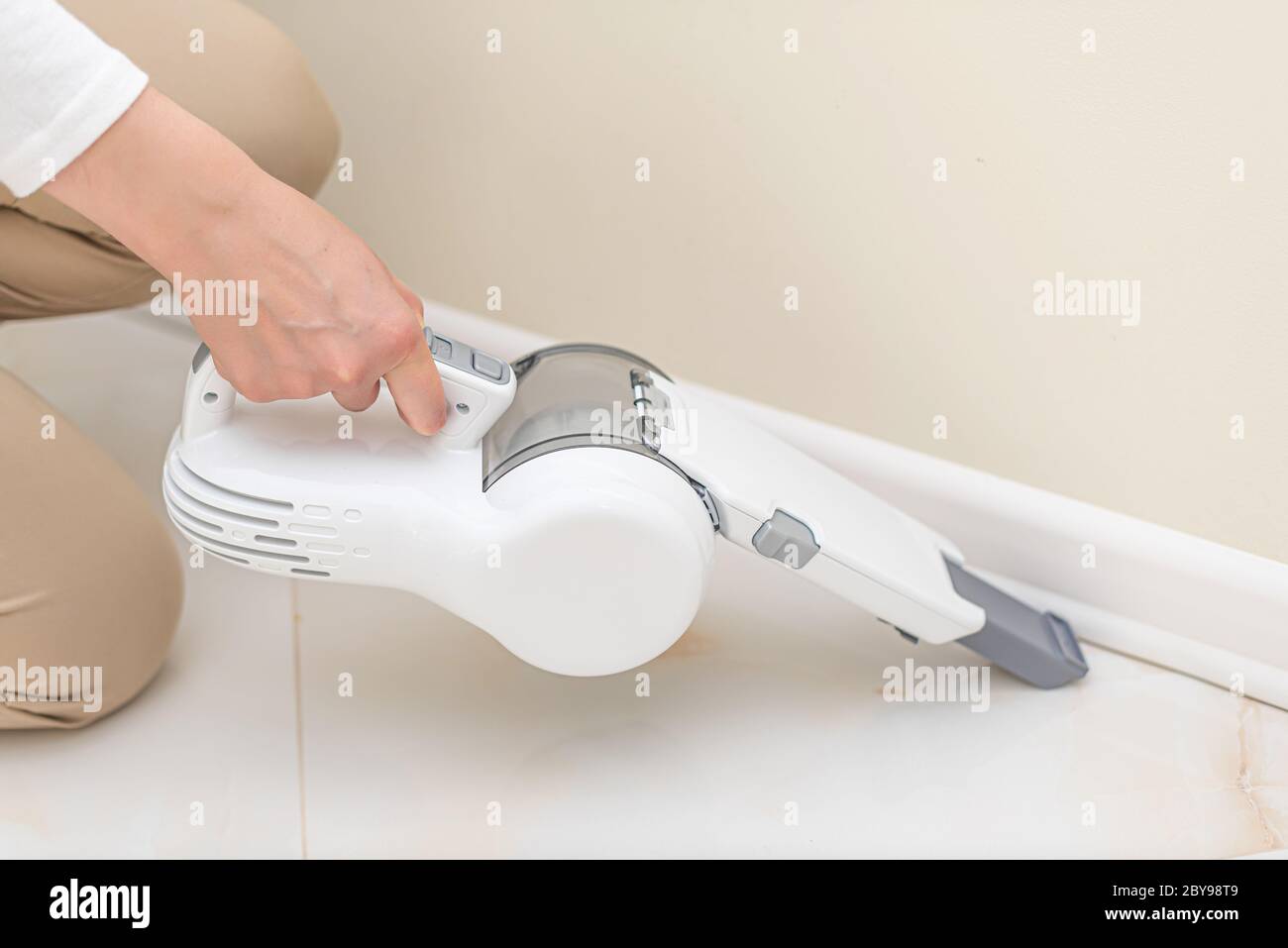 Woman vacuuming furniture in a house with a hand-held portable vacuum ...