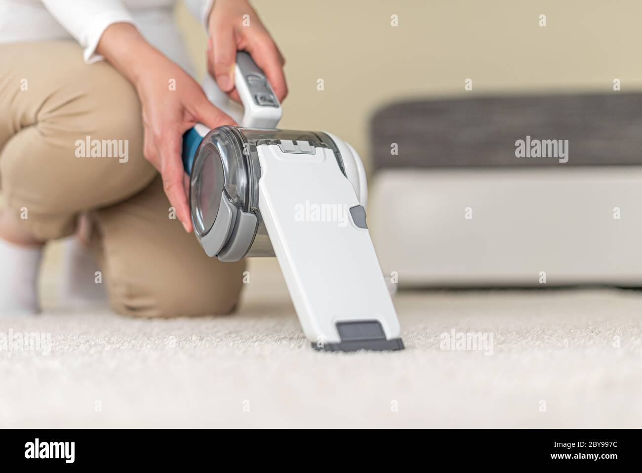 Woman vacuuming furniture in a house with a hand-held portable vacuum ...