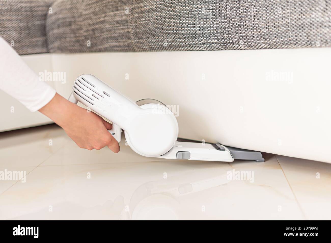 Woman vacuuming furniture in a house with a hand-held portable vacuum ...