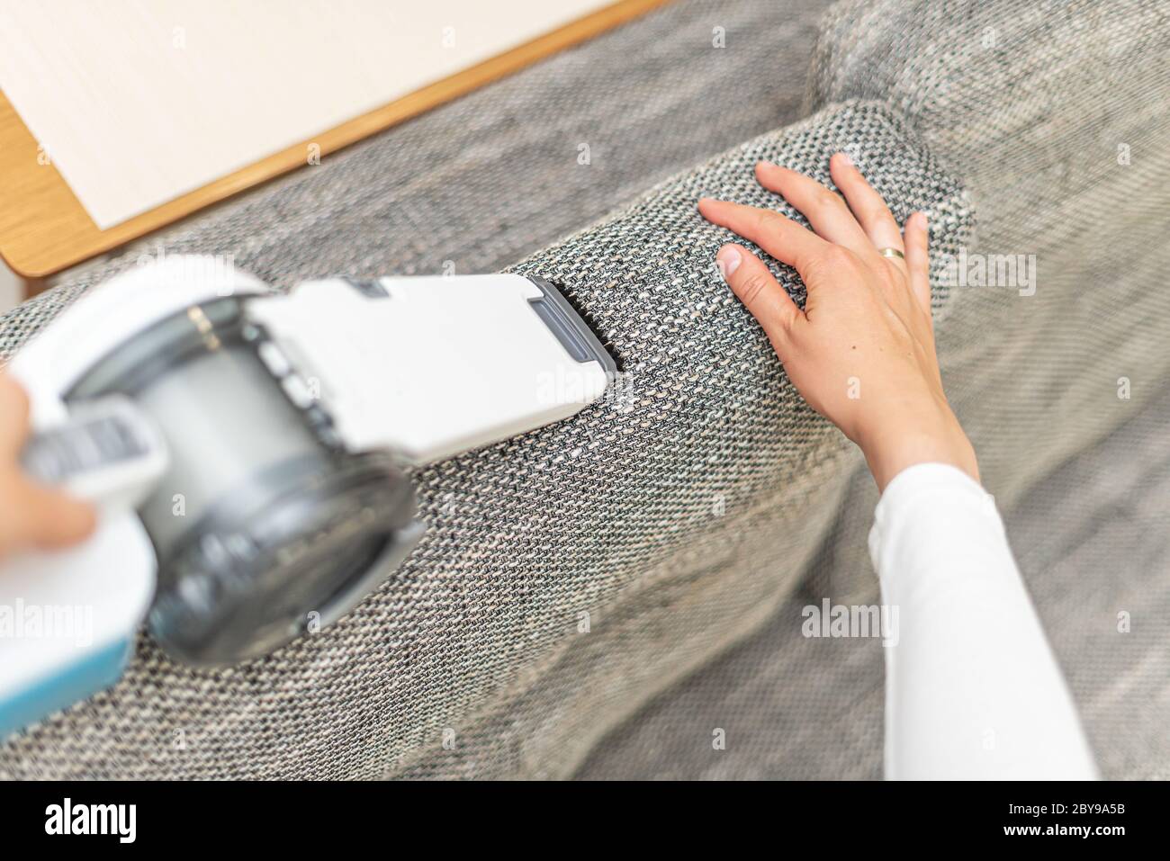 Woman vacuuming furniture in a house with a hand-held portable vacuum ...