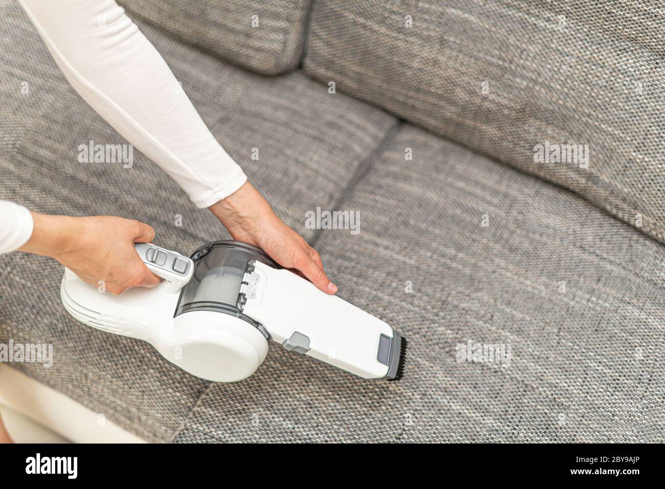 Woman vacuuming furniture in a house with a hand-held portable vacuum ...