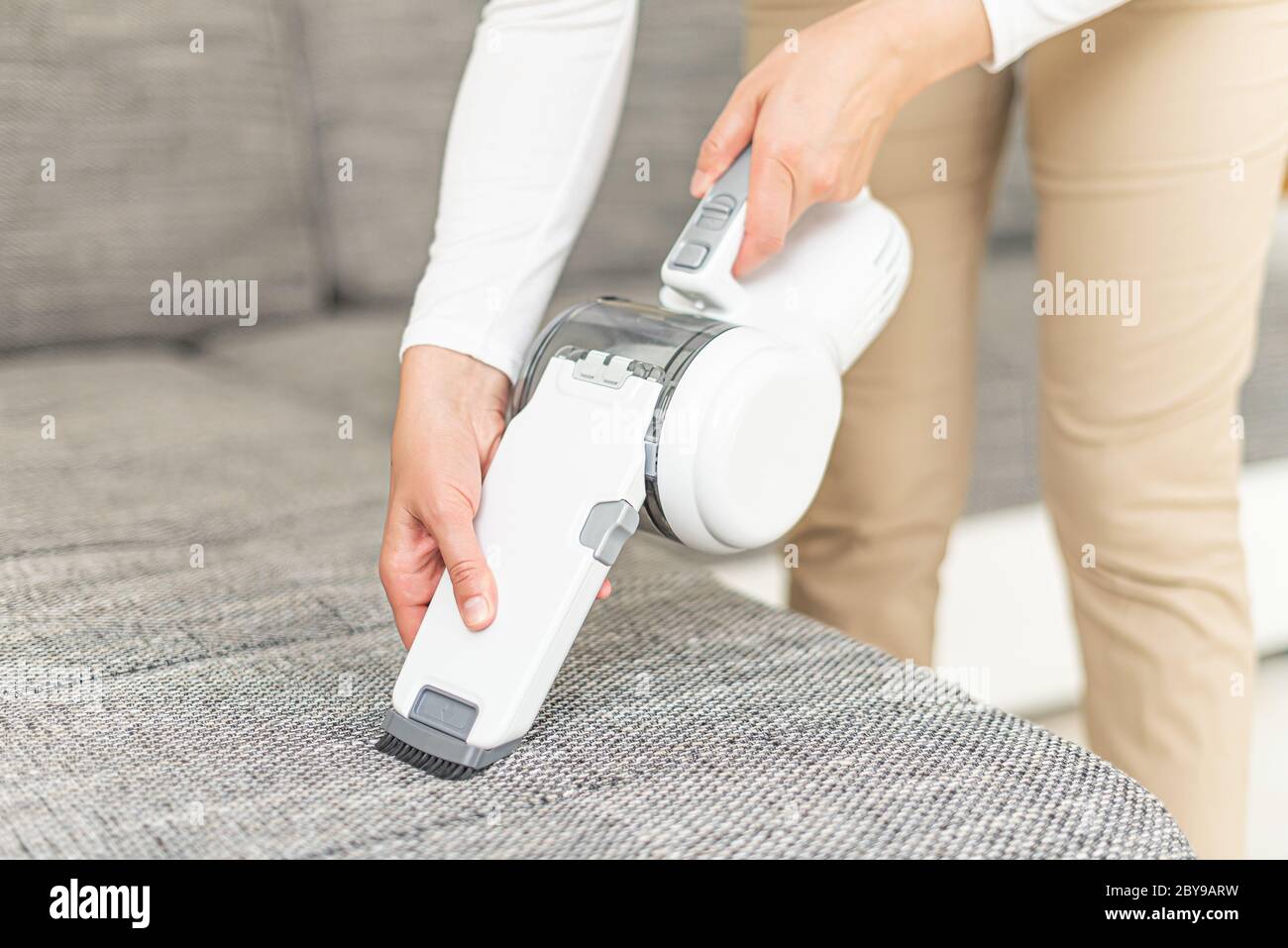 Woman vacuuming furniture in a house with a hand-held portable vacuum ...