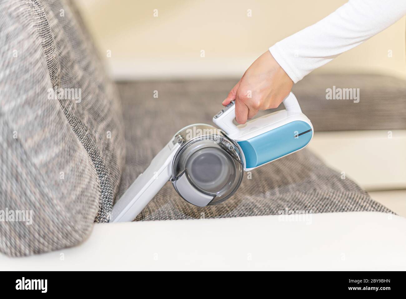 Woman vacuuming furniture in a house with a hand-held portable vacuum ...