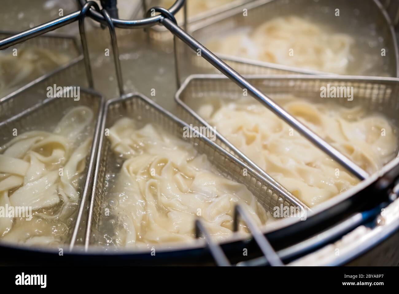 Thick chinese noodles boiling in a hot water in a street food take away ...