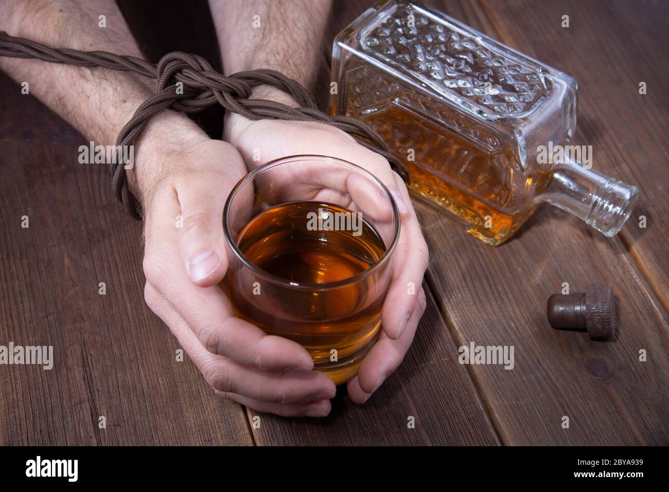 Tied male hands with a glass and a bottle of alcohol. The concept of ...