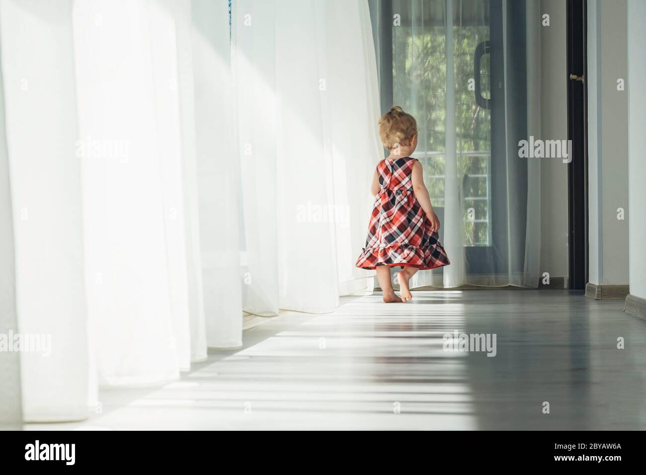 Baby girl in a beautiful dress walking along the corridor. Back view ...