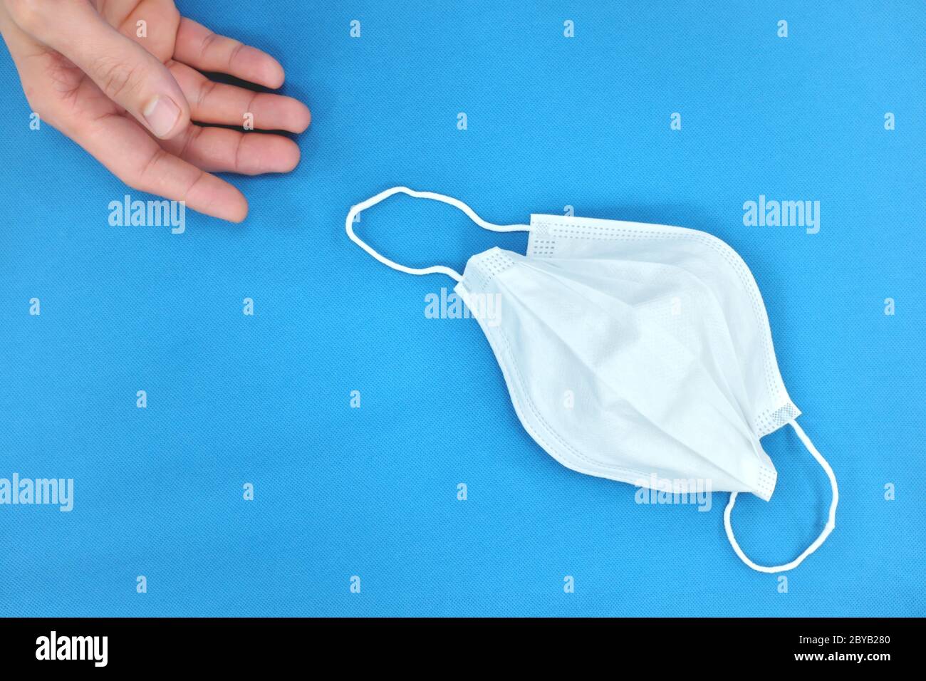 Male hands laying down white face mask on table. Blue background, flat ...