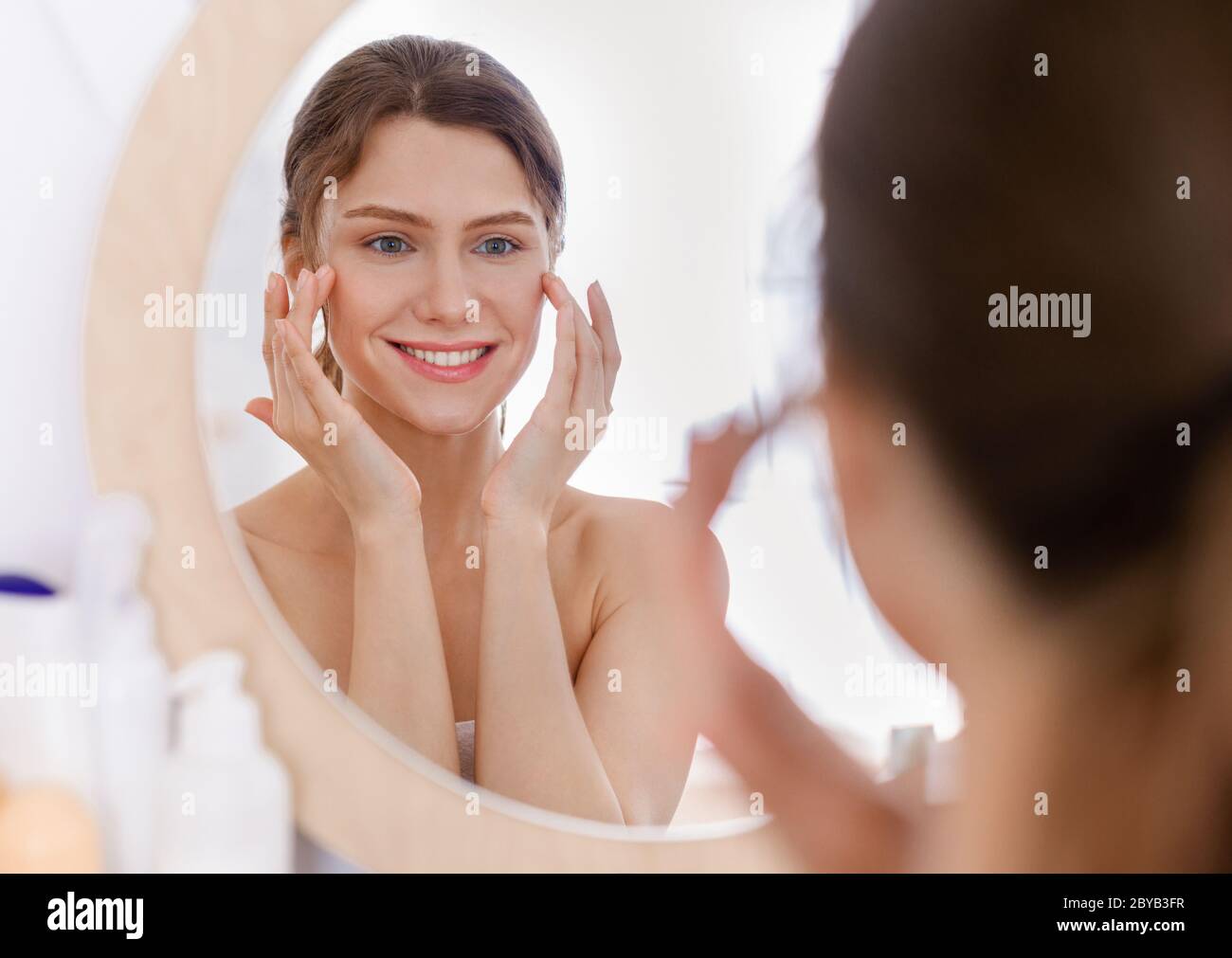 Beautiful woman looking at mirror and applying eye serum Stock Photo ...