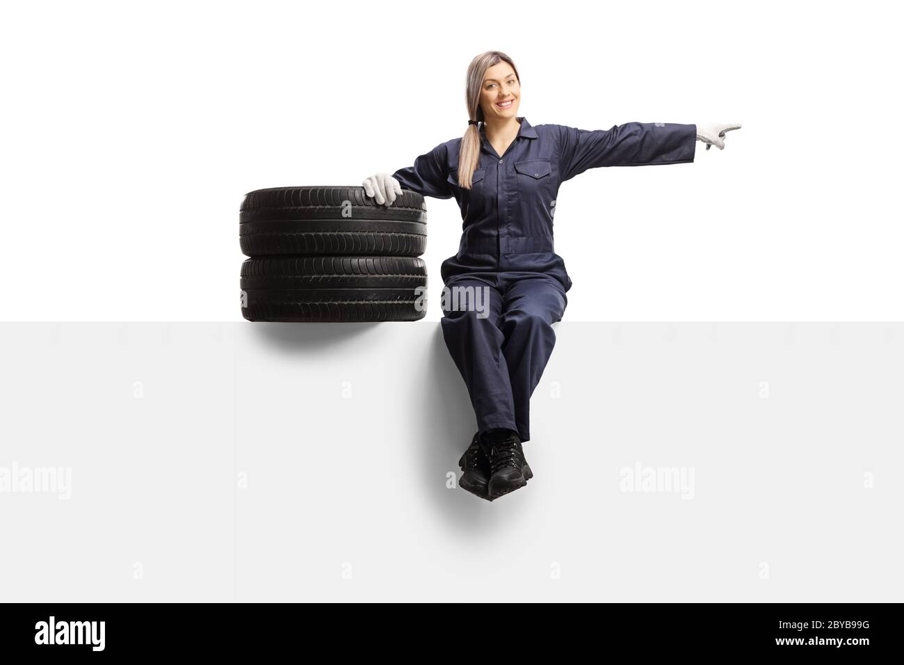 Female auto mechanic sitting on a panel with tires and pointing to the ...