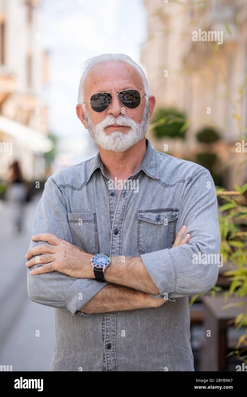 Happy rich old man with beard and sun glasses on street posing and ...