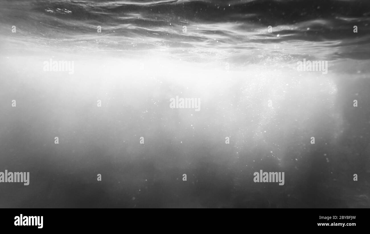 Black and white image of sun rays and floating air bubbles in sea water ...