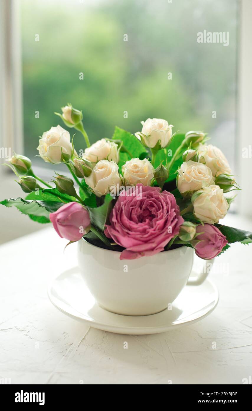 A bouquet of white roses in a cup on a white table opposite the window ...