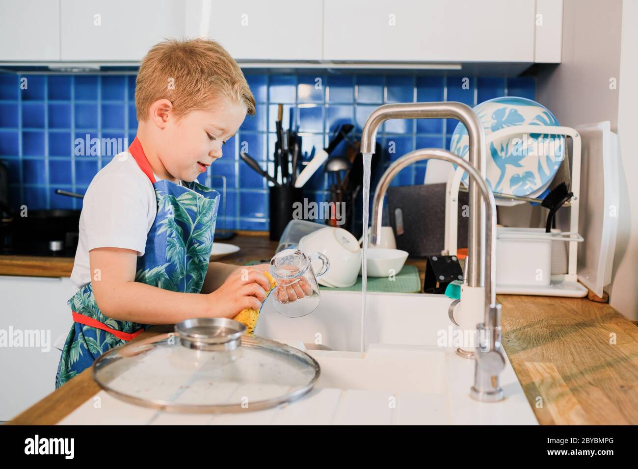 a boy in an apron washes dishes in the kitchen at home Stock Photo - Alamy