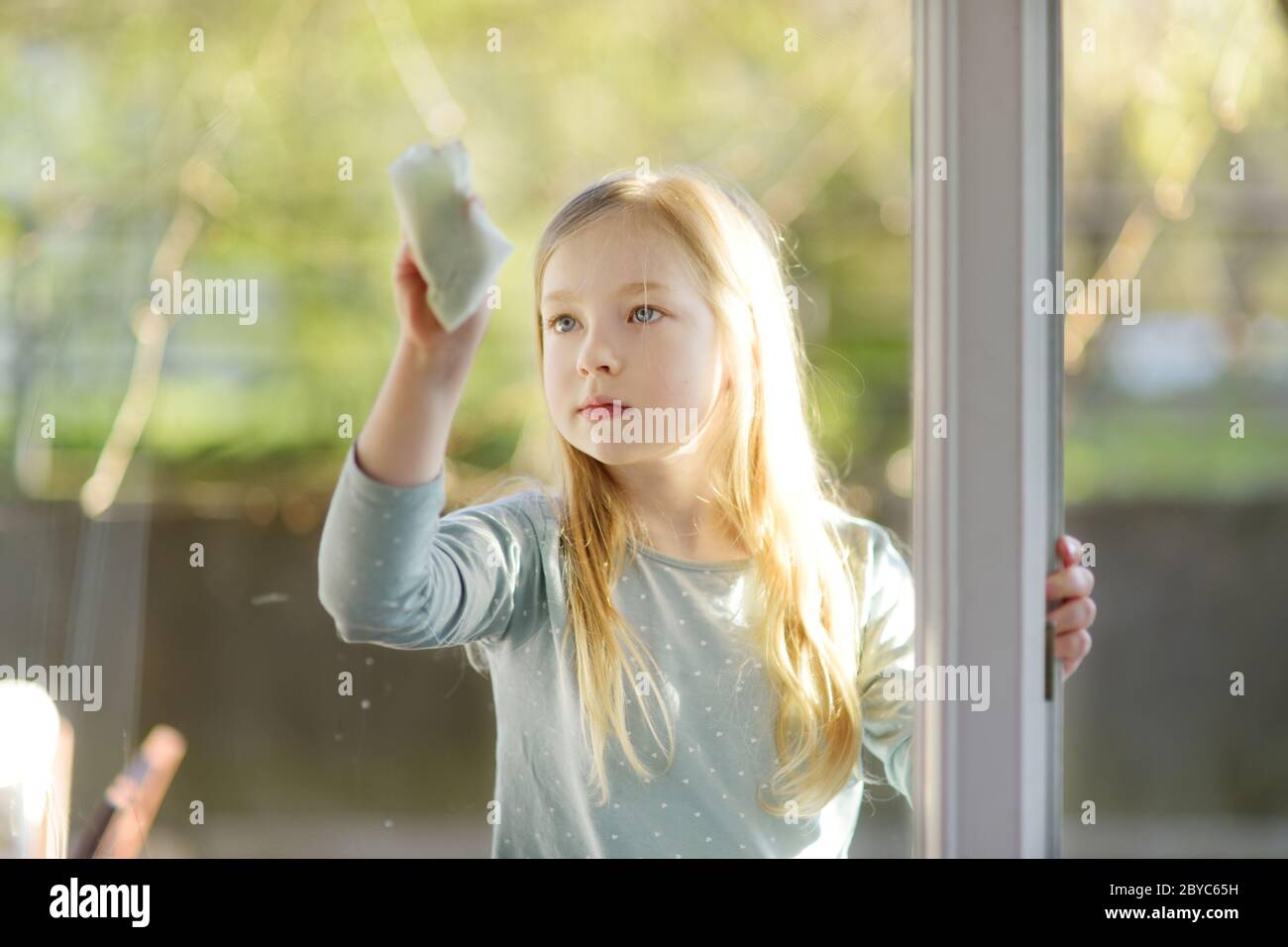 Cute young girl cleaning a window with paper cloth. Child helping with ...