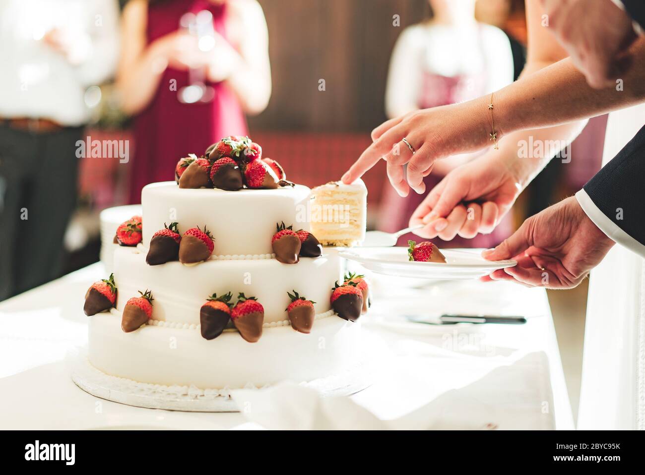 Bride slicing white wedding cake decorated with strawberries and ...