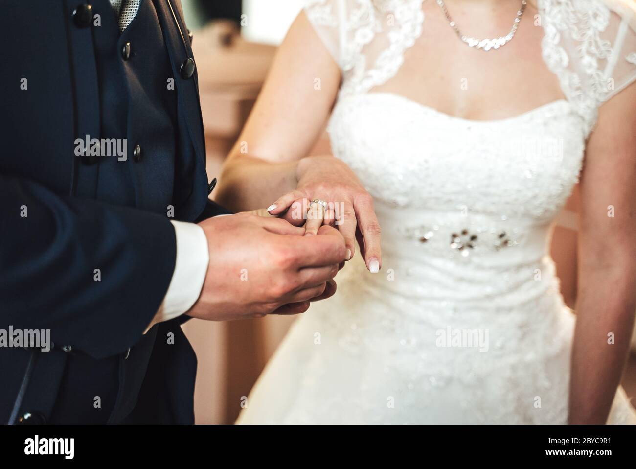 Close up of groom putting wedding ring on bride's finger. Bride and ...