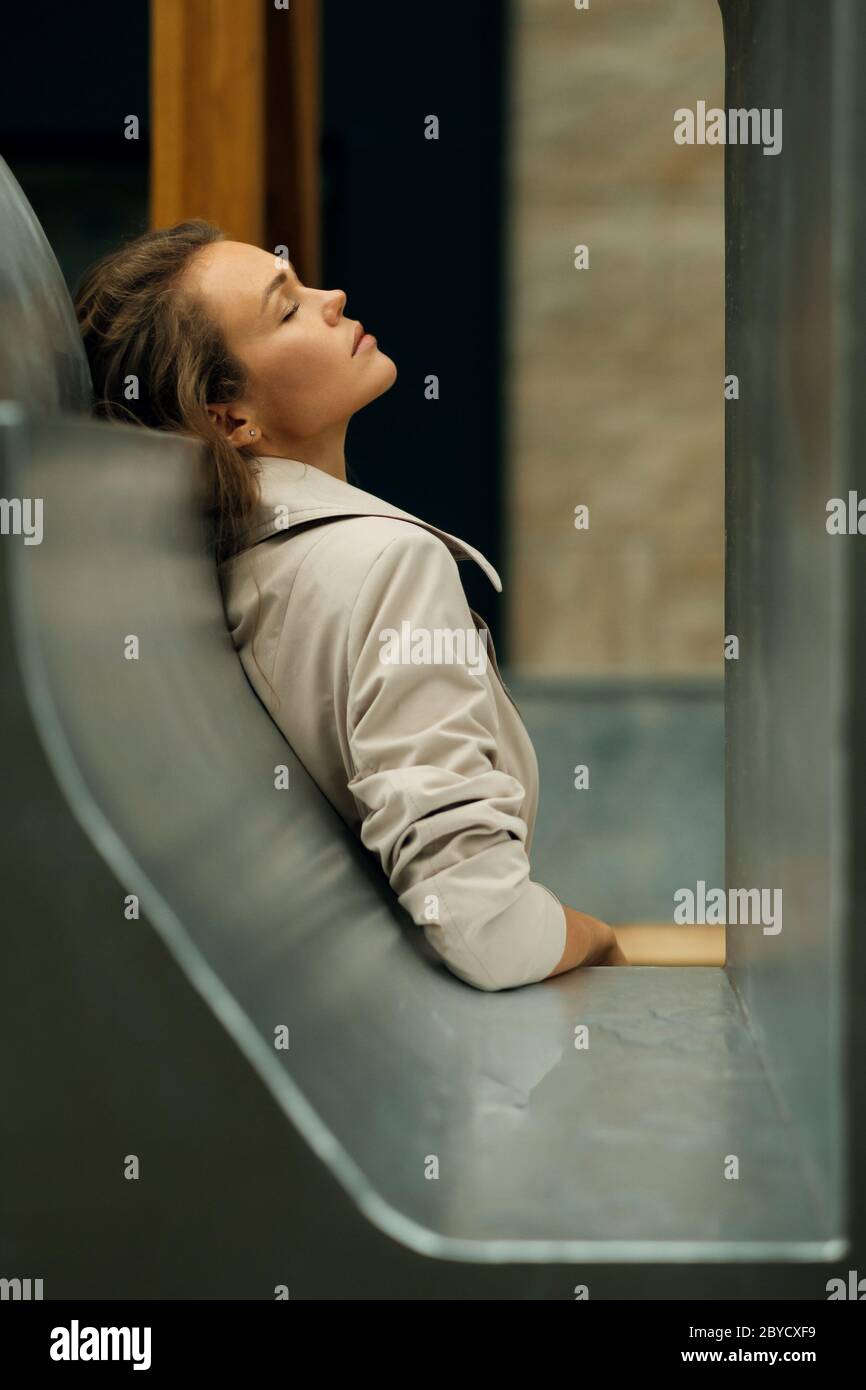 Attractive young lady wearing gray trench coat lean on architectural ...
