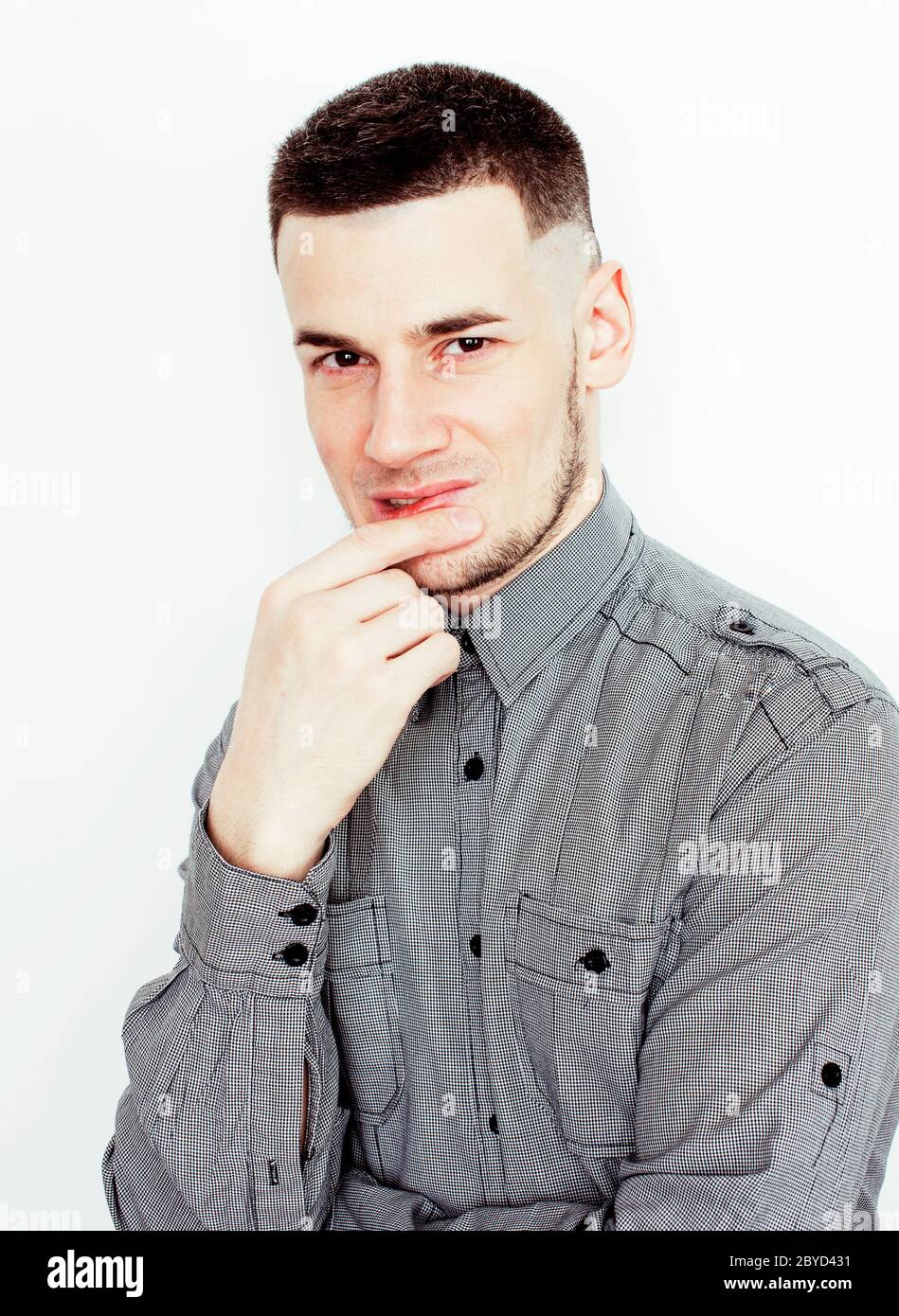 Portrait of a smart serious young man standing against white background ...