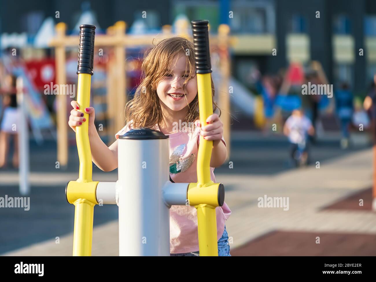 Cute little girl sports on the playground on an elliptical trainer ...