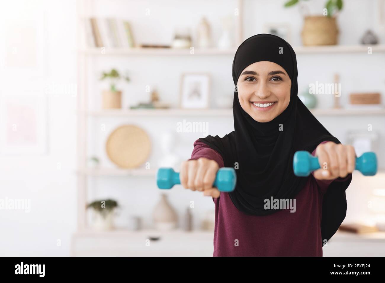 Smiling muslim girl in hijab exercising with dumbbells at home Stock ...