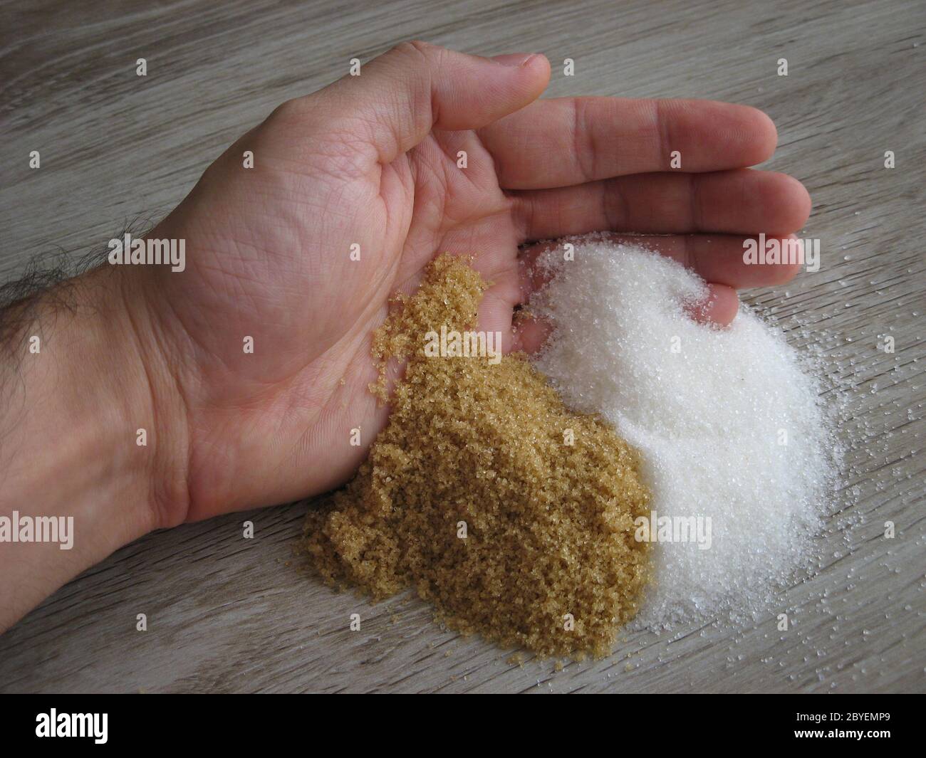 White and brown sugar on male hand with wooden background. Brown and ...