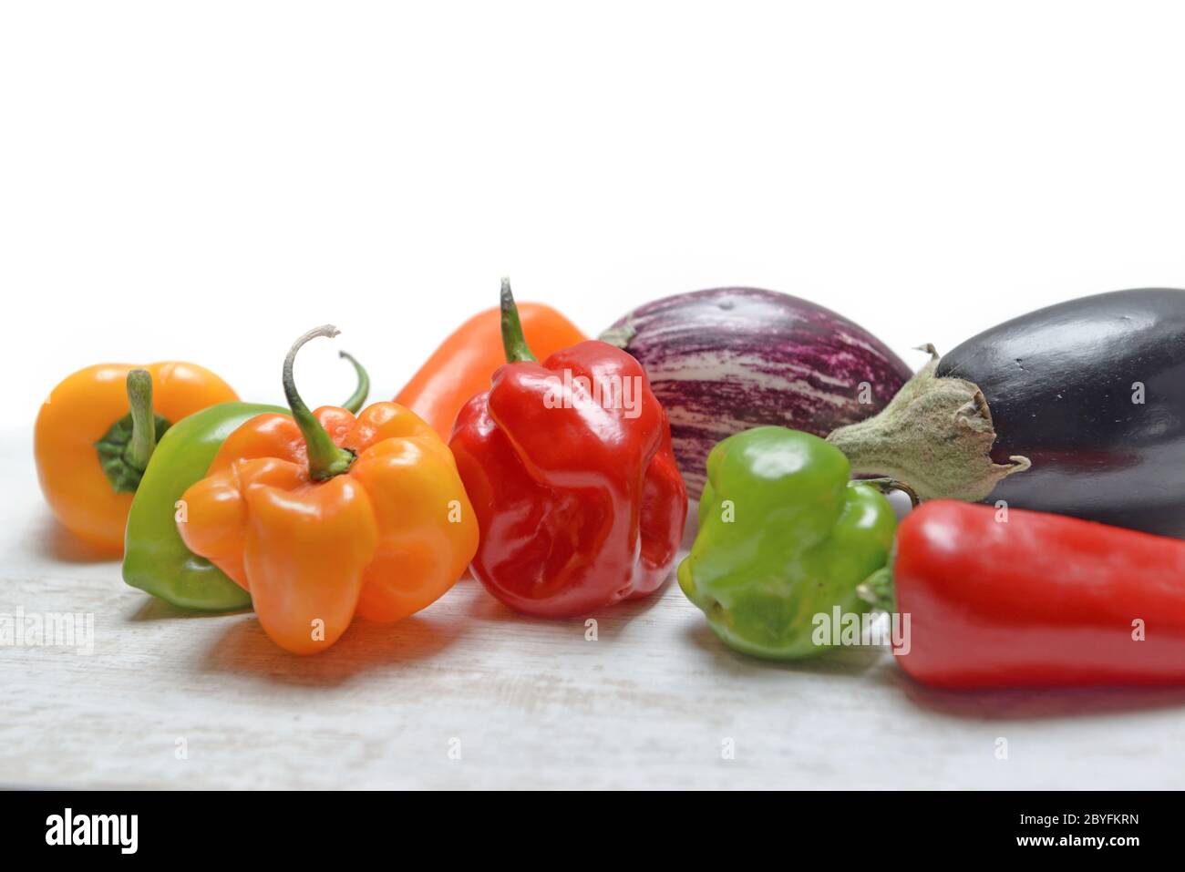 group of colorful hot peppers and eggplant on a table and white ...