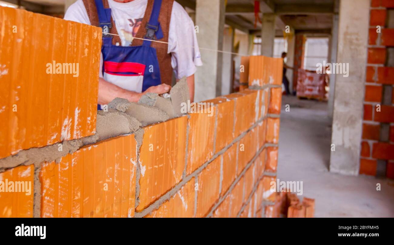 Mason, bricklayer worker is using red blocks to mount a wall next the ...