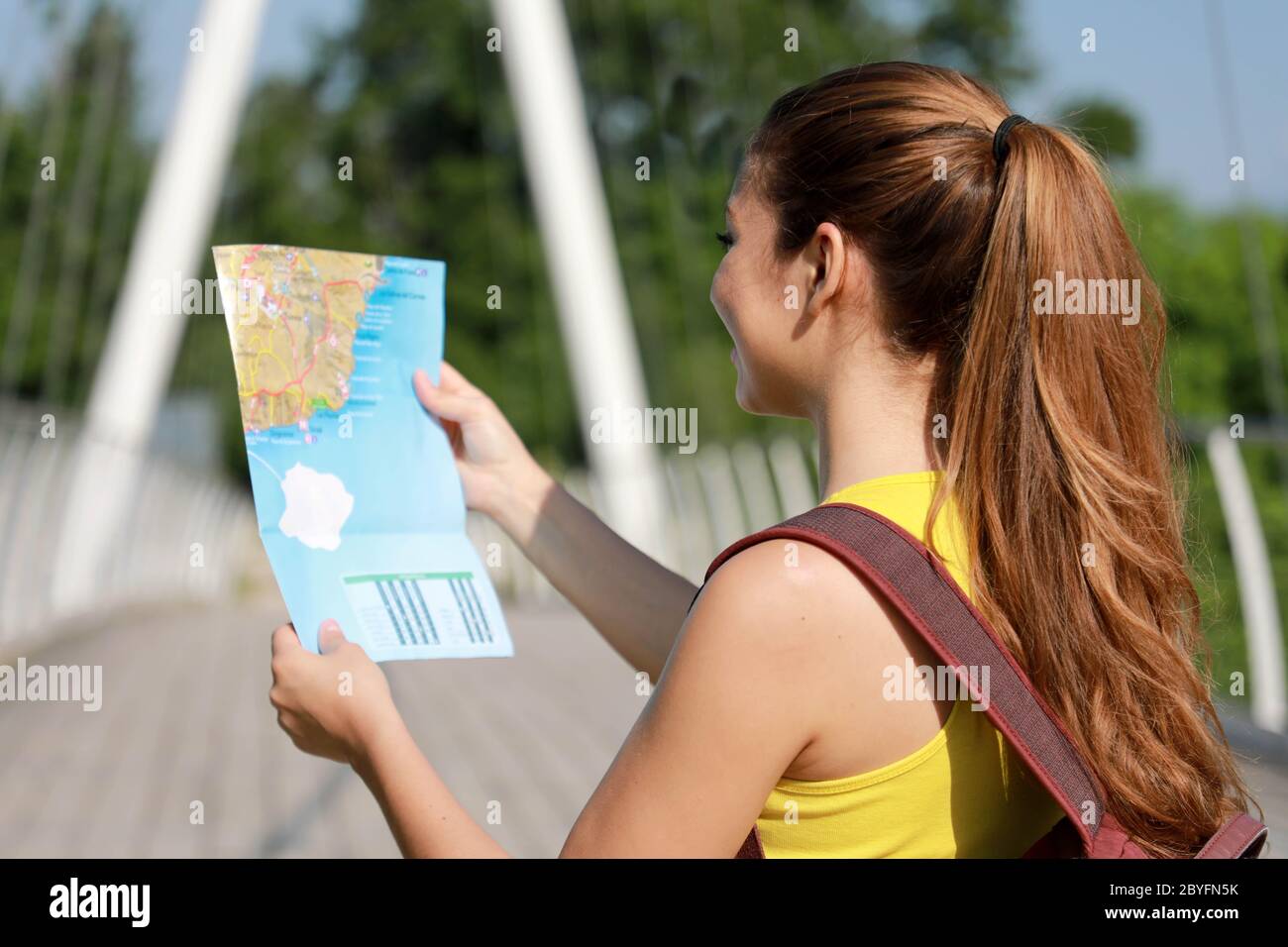 Back view of young female backpacker looking at a map on bridge in the ...