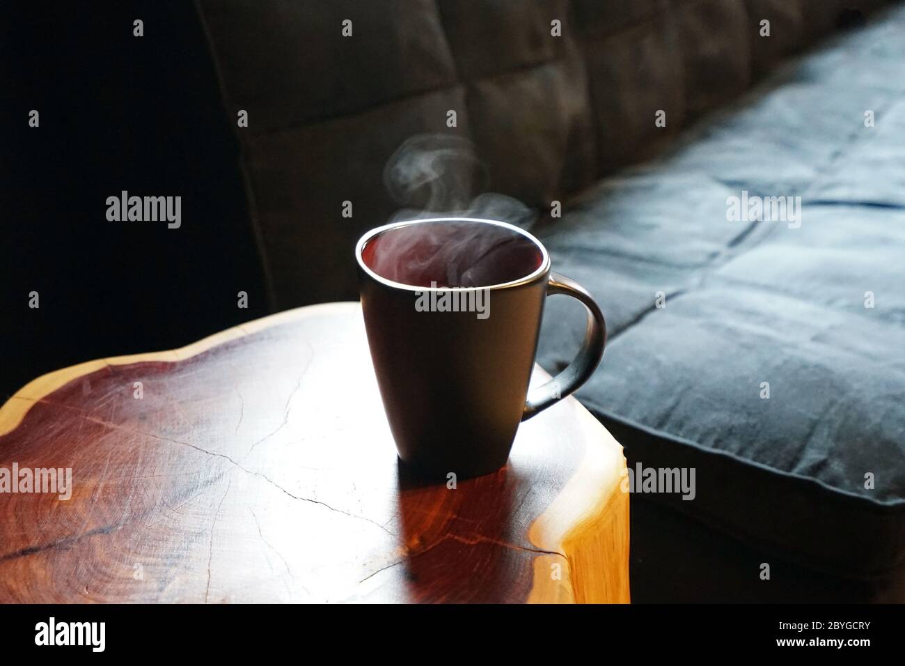 A mug of hot coffee on wooden stool table with cushion sofa on the back ...