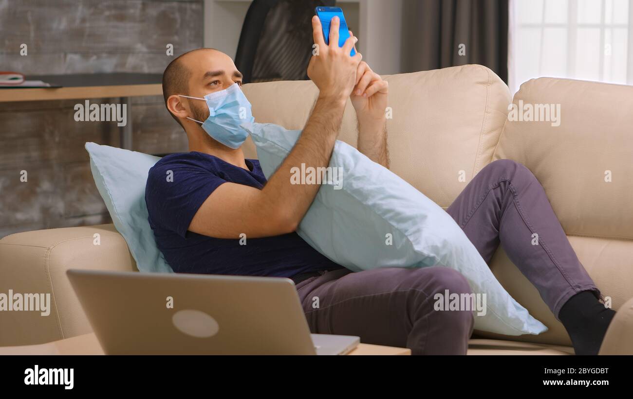 Bored man with protection mask during covid-19 browsing on social media ...