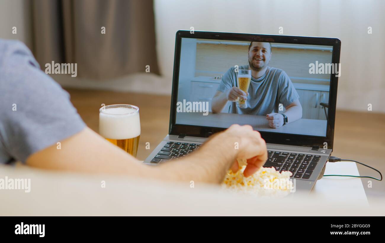 Back view of happy man on video call with his friend drinking beer ...