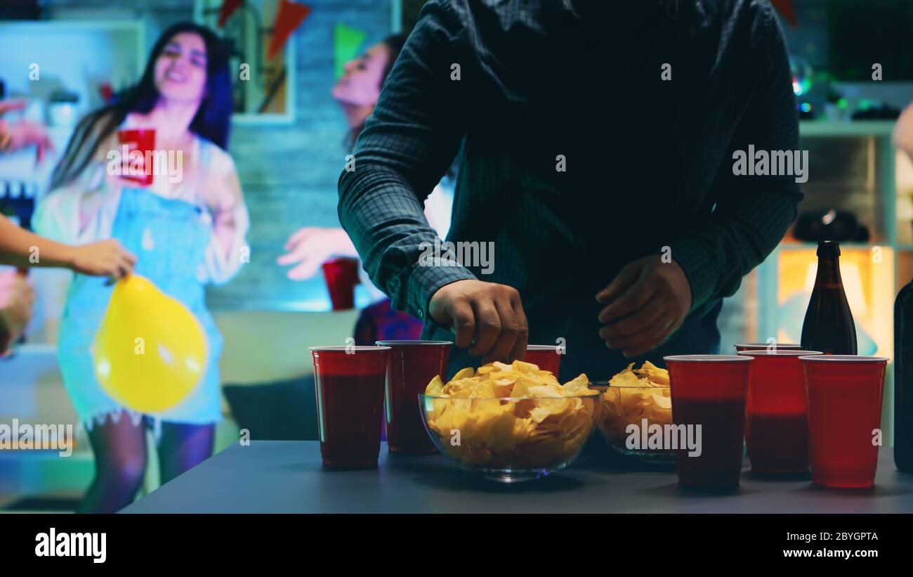 Young man taking chips from the table while his friends are dancing at ...