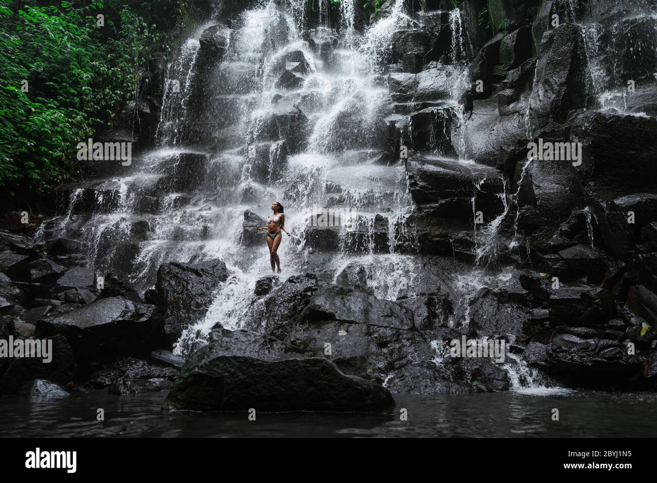 Amazing woman enjoying under stream of big and beautiful cascade ...