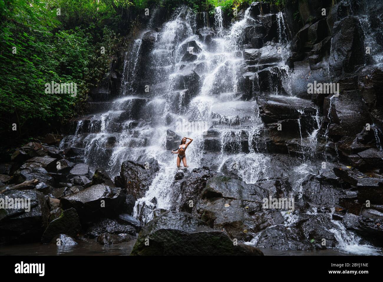 Amazing woman enjoying under stream of big and beautiful cascade ...