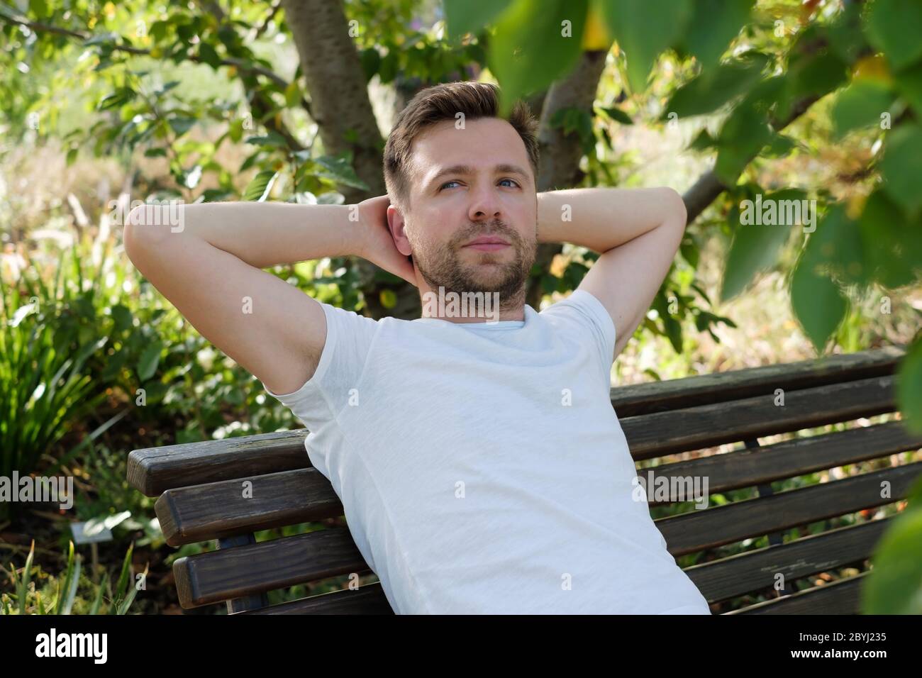 Caucasian young man sitting on a bench in the park and having a rest ...