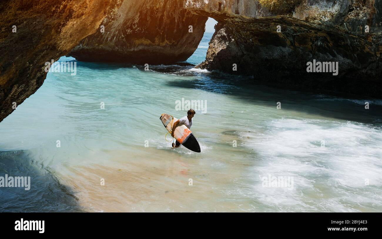 Young surfer sport man carrying his surfing board and going out the ...